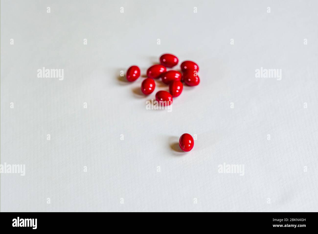 A small heap of red medical tablets, one tablet separated, displayed on ...
