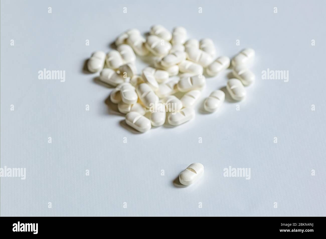 A small heap of white medical tablets, one tablet separated, displayed ...