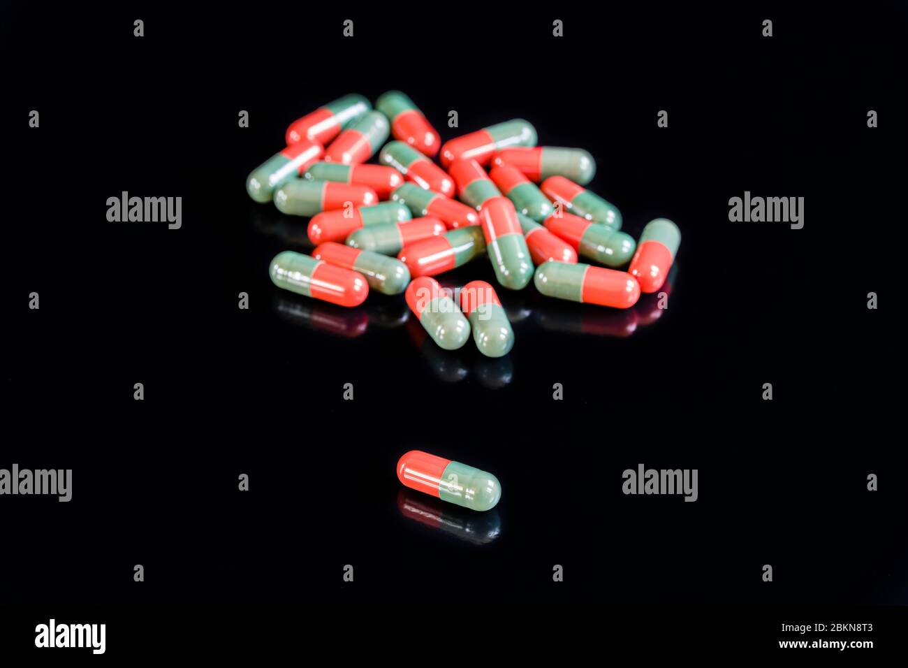 A small heap of red and green medical capsules, one capsule separated ...