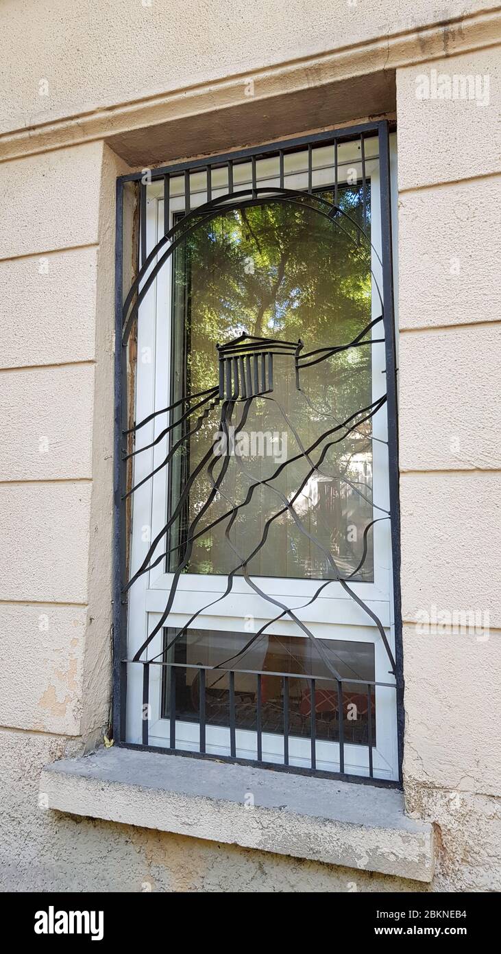 Ornate metal grating protected white window with blurry reflection in ...