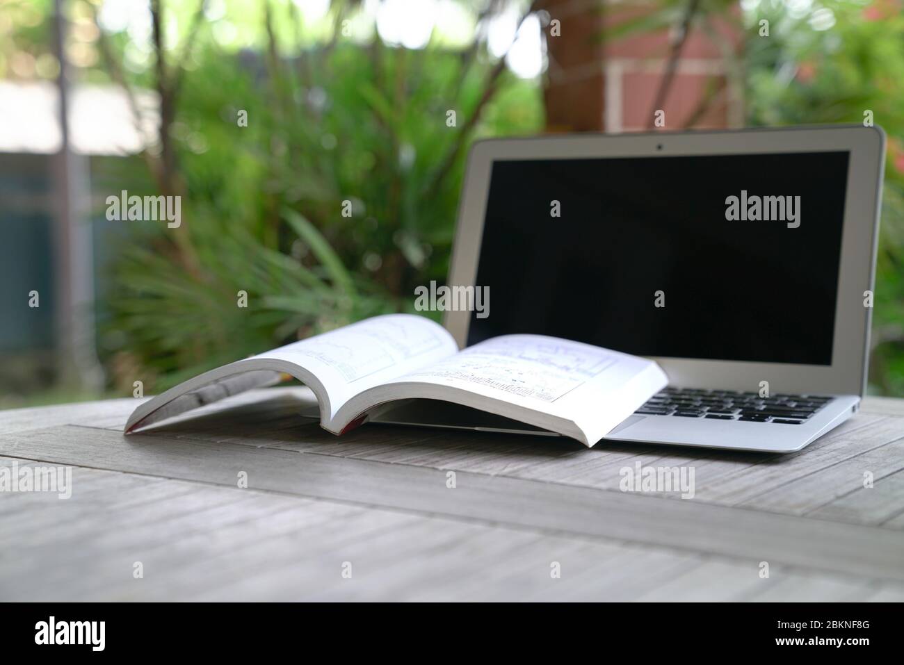 Open book on top of computer laptop. Garden view. Home setting. Onlien ...