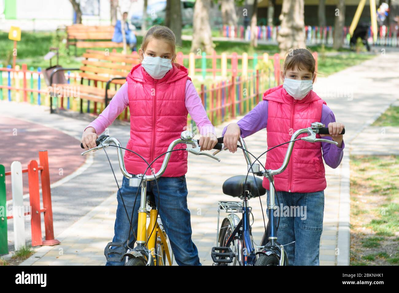 Two girls with medical masks on their face walk with bicycles in the ...