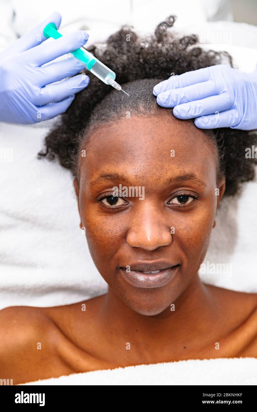 Doctor aesthetician makes head beauty injections to a female african ...