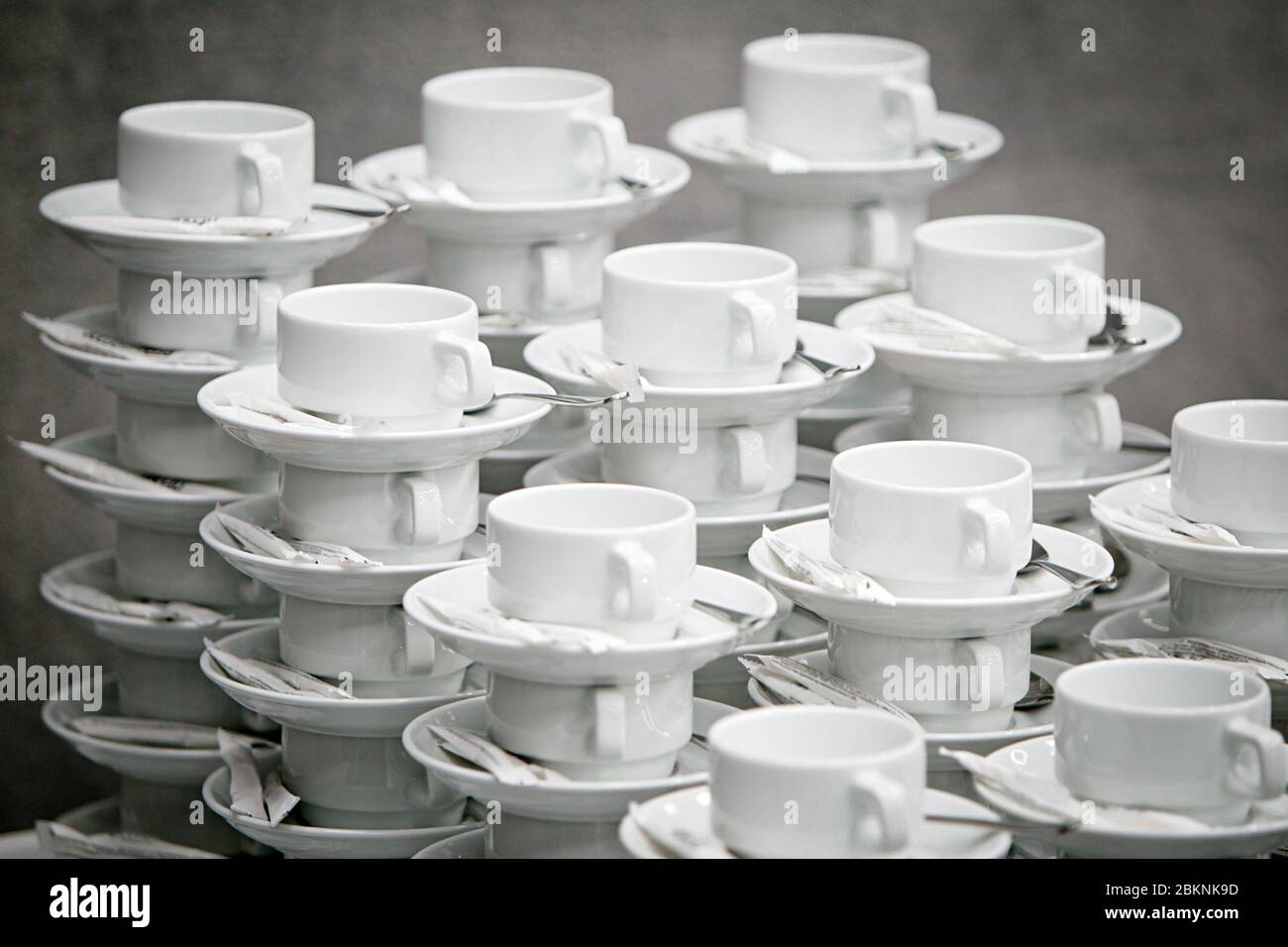 Piles of empty white ceramic cups with saucers, teaspoons and sachets ...