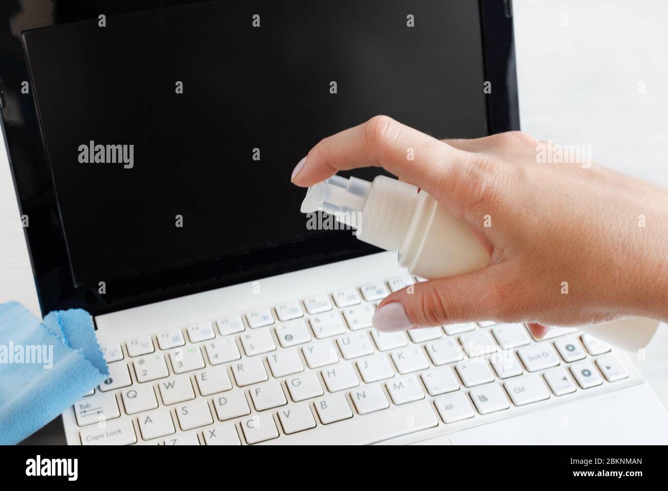 Woman hand disinfecting computer keyboard with antibacterial cleanser ...