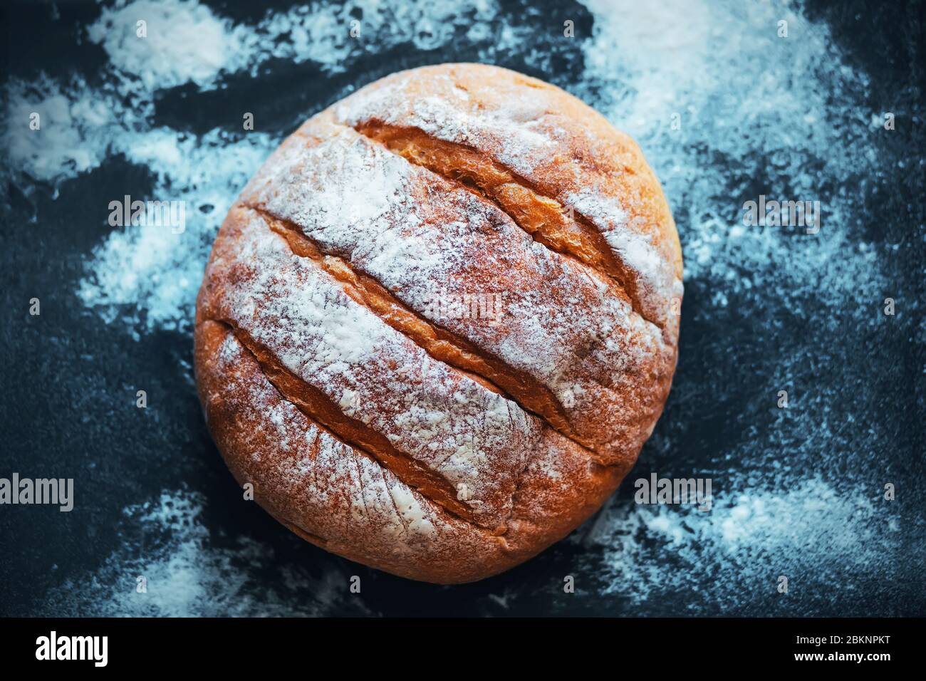 Fresh, warm, round, homemade bread made from wheat flour lies on a dark ...