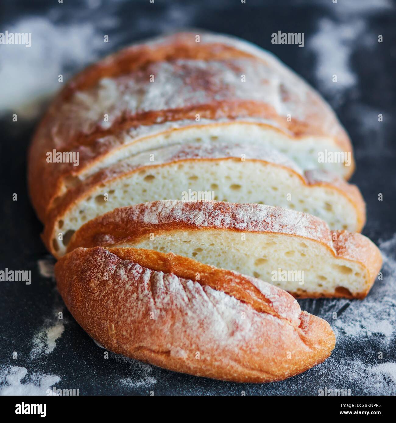 Delicious homemade wheat bread, cut into pieces, lies on a black tray ...