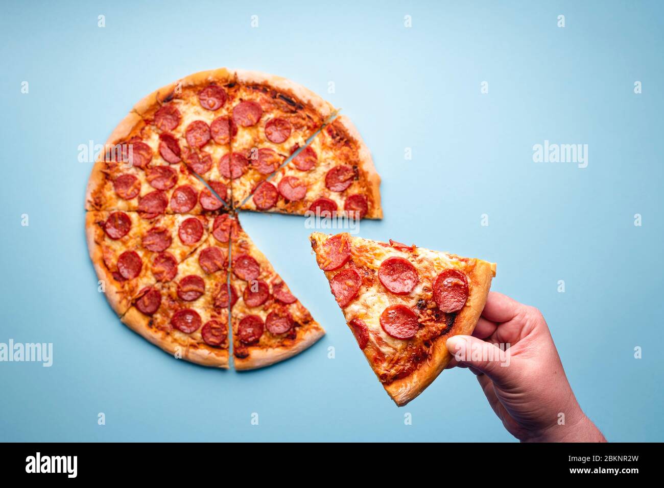 Above view with woman's hand taking a slice from a pepperoni pizza ...