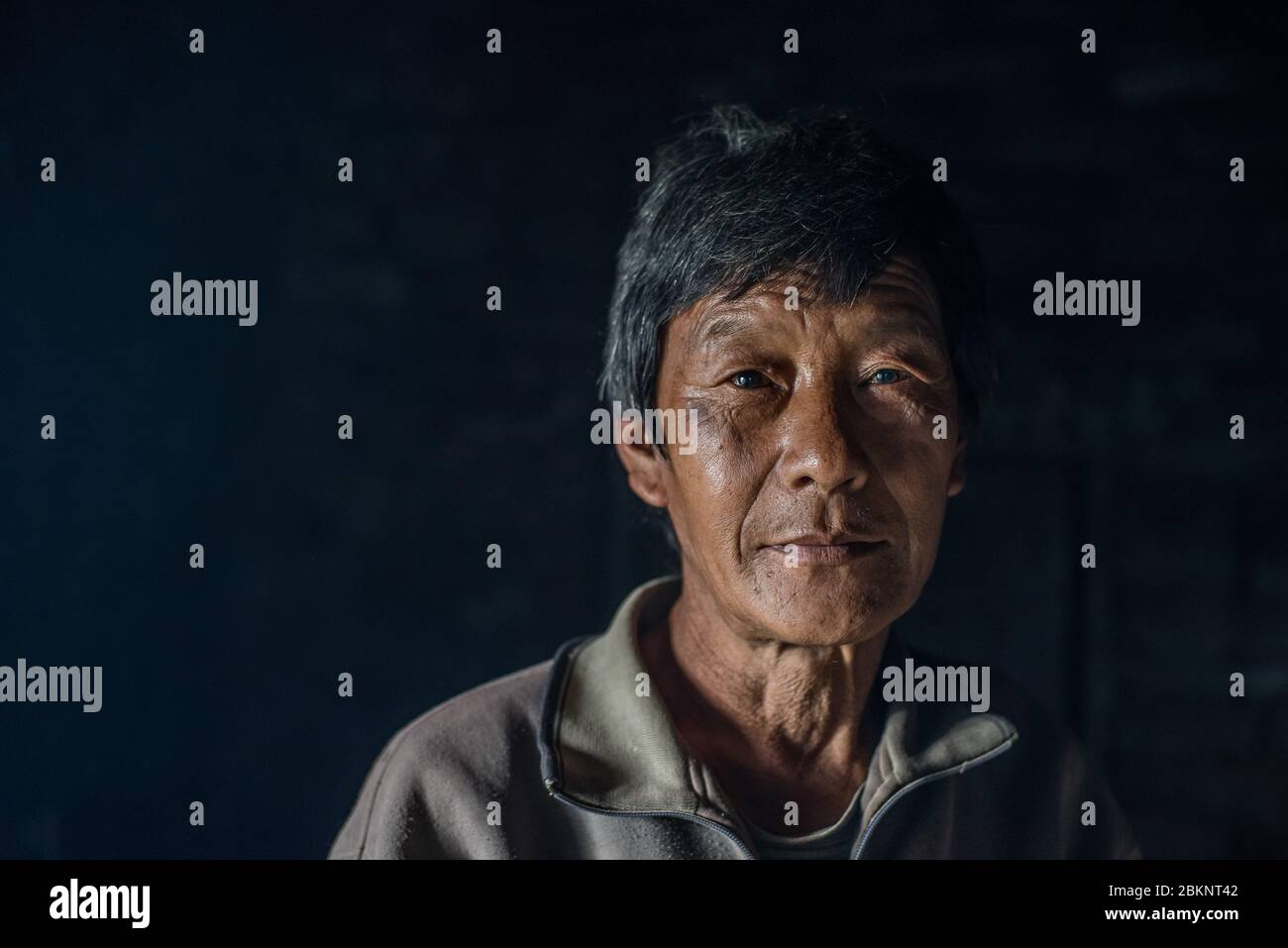 Portrait of a mature Indian man. Naturally side lit in dark interior ...