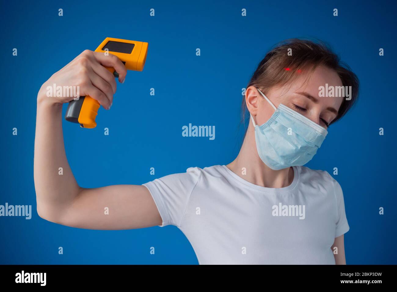 Woman in medical face mask holding yellow pyrometer and showing suicide ...
