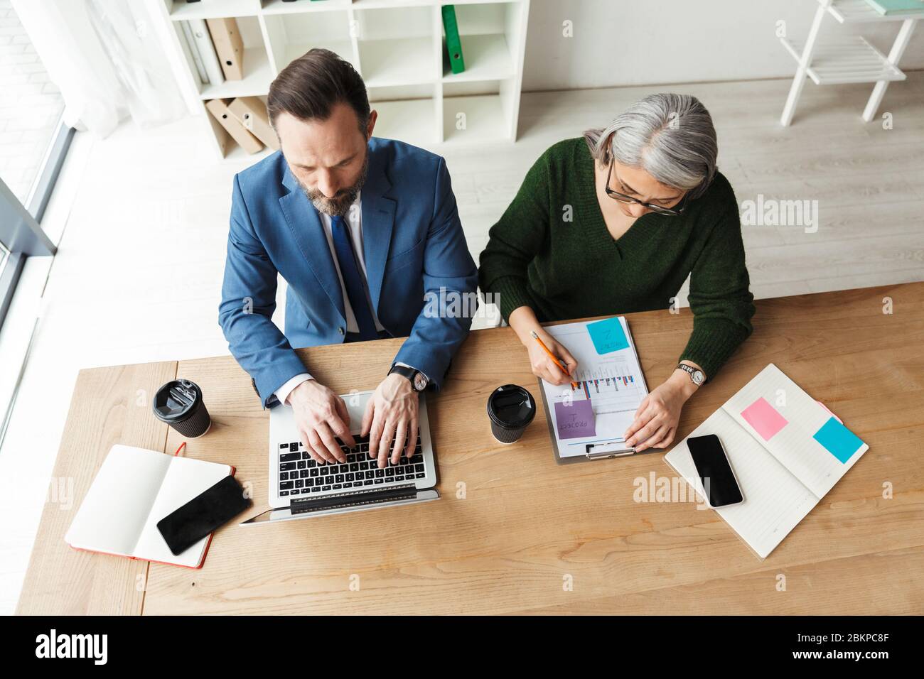 Photo of adult focused colleagues talking while working with laptop and ...