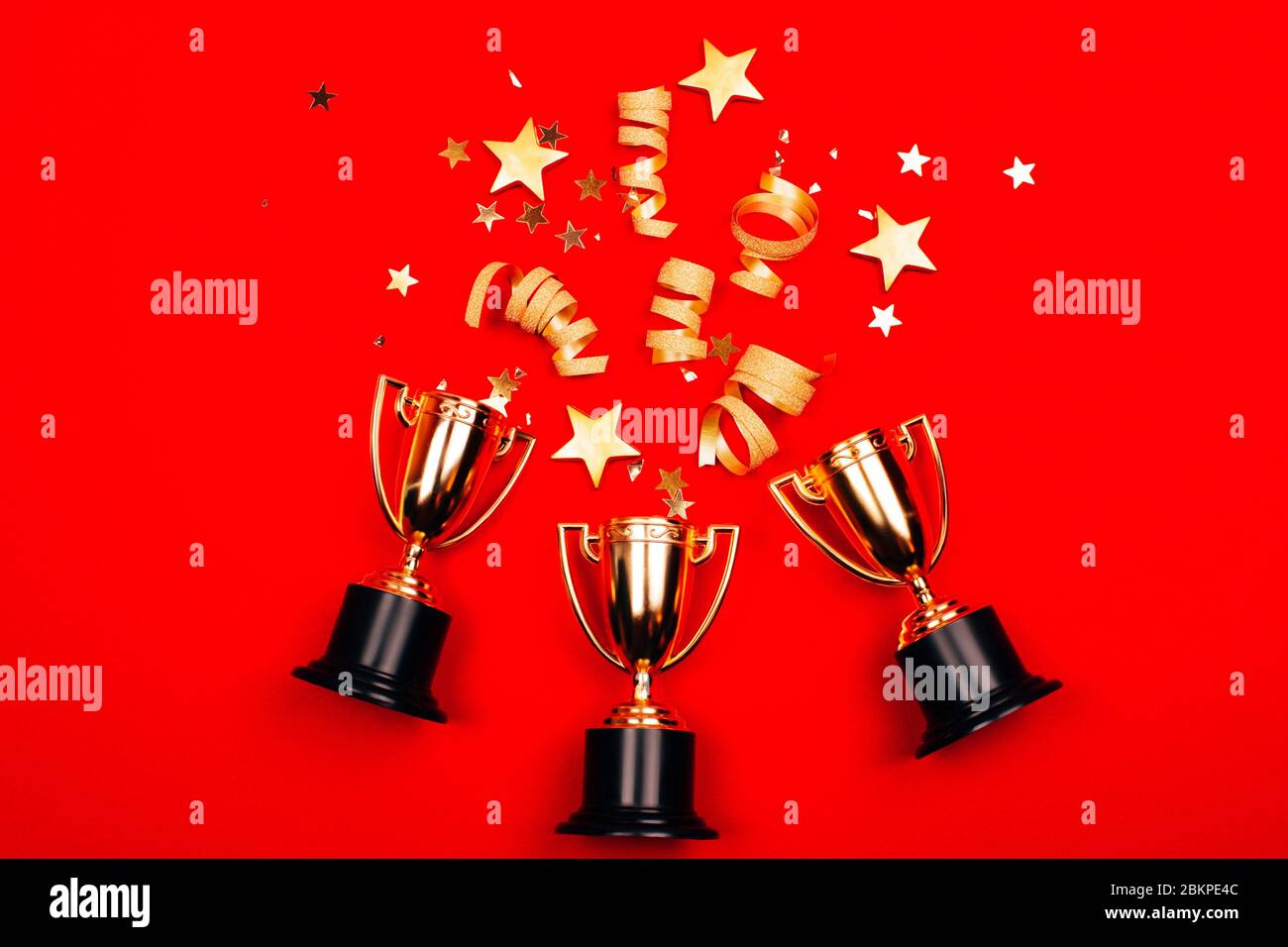 Three golden winner cups with confetti on a red background. Flat lay ...