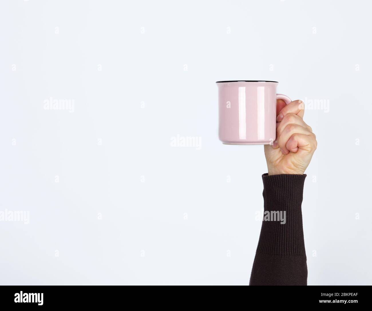 pink ceramic cup in a female hand on a white background, hand is raised ...