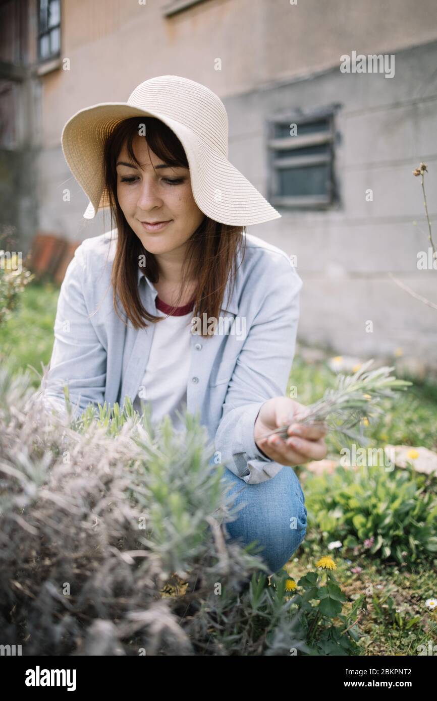 Florist woman squatting in yard and tearing plants. Girl picking ...