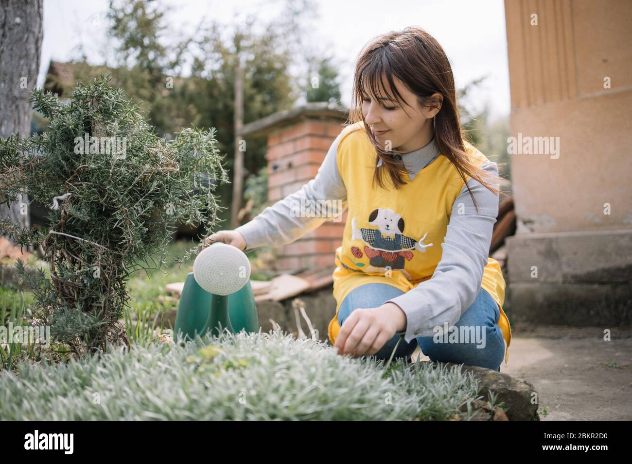 Woman sitting in yard and holding watering can. Young woman caring ...