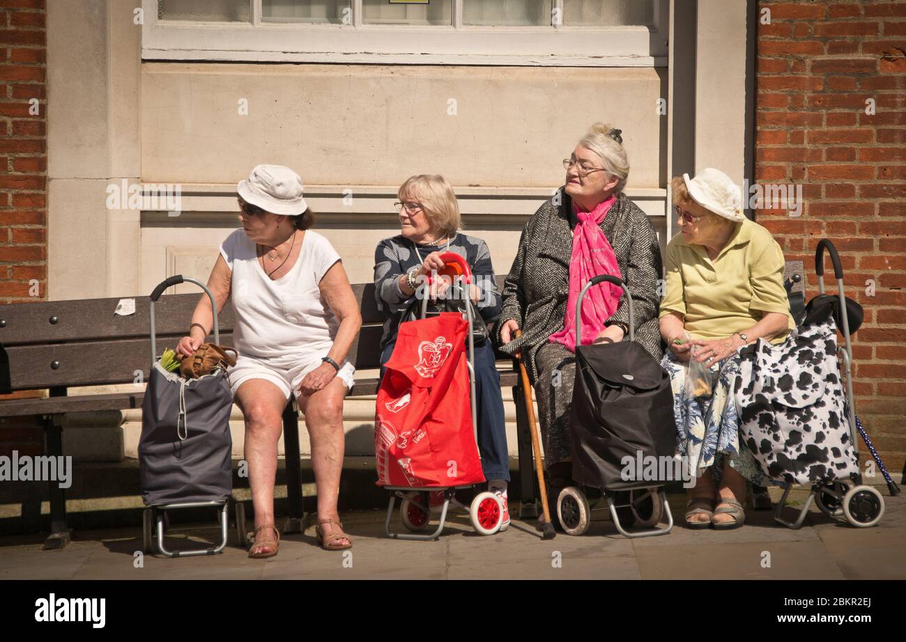 Ladies sat on seat by a bus stop looking to the left to see if the bus ...