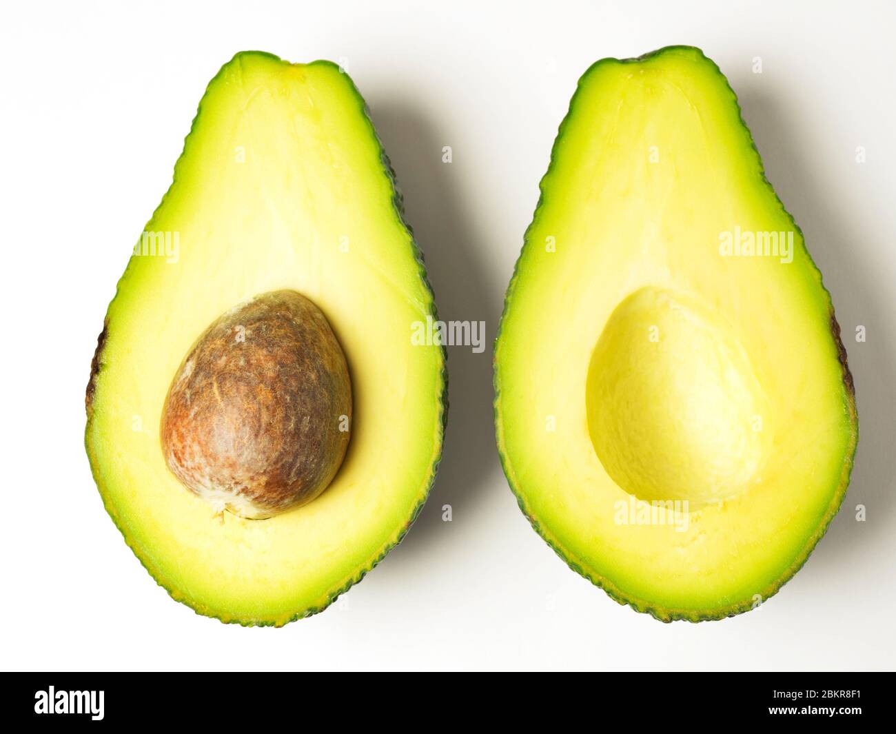 Two avocado halves the same way up with the stone left in one half on a ...
