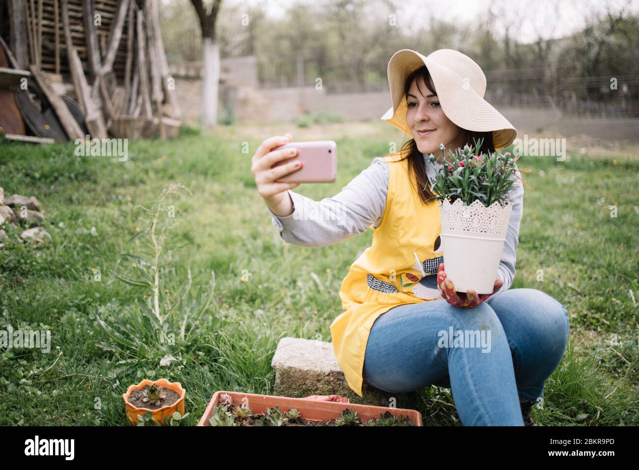 Happy girl holding pot with flower and taking selfie. Smiling woman ...