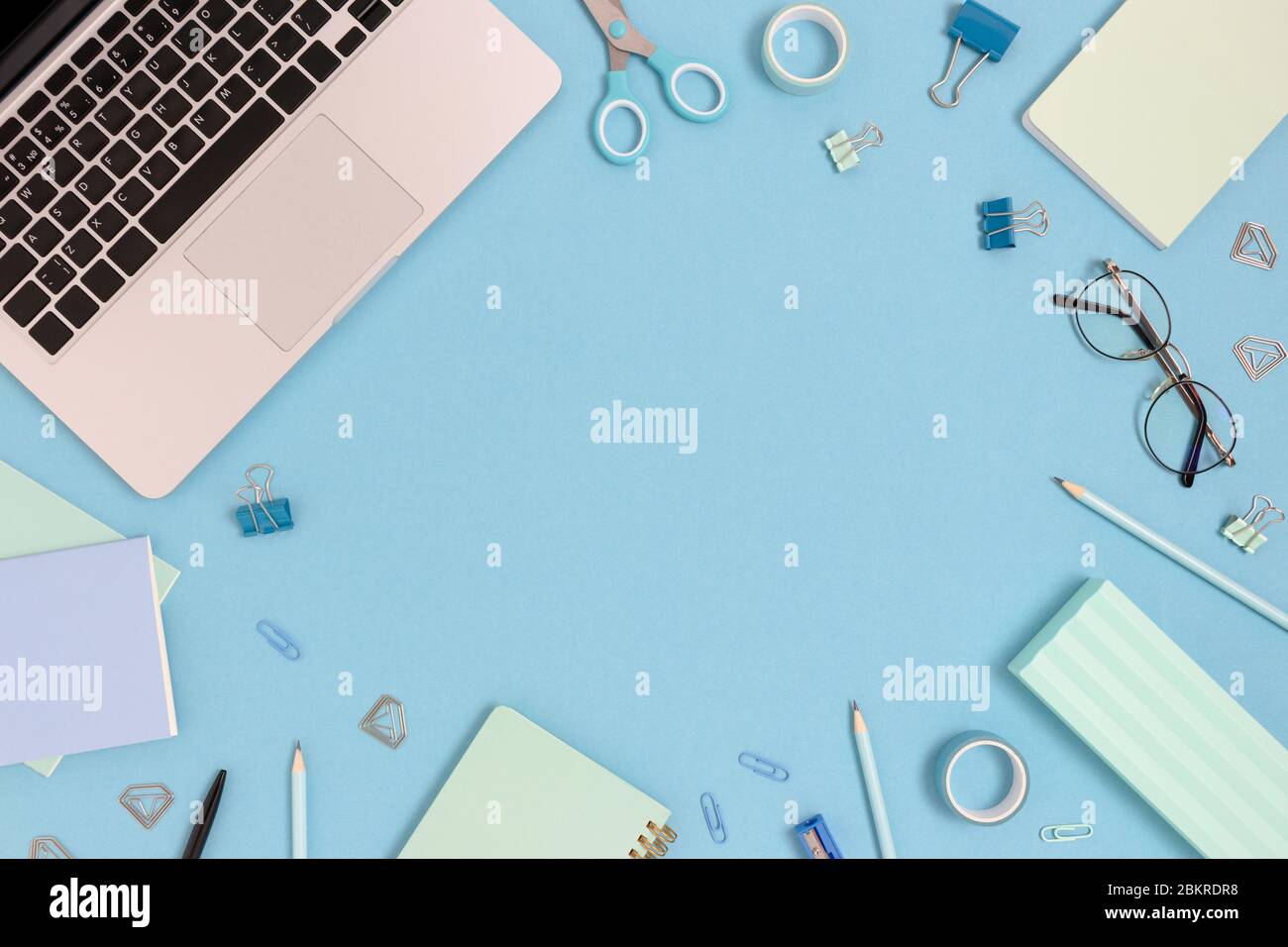 Frame made of laptop, glasses and stationery on a blue pastel ...