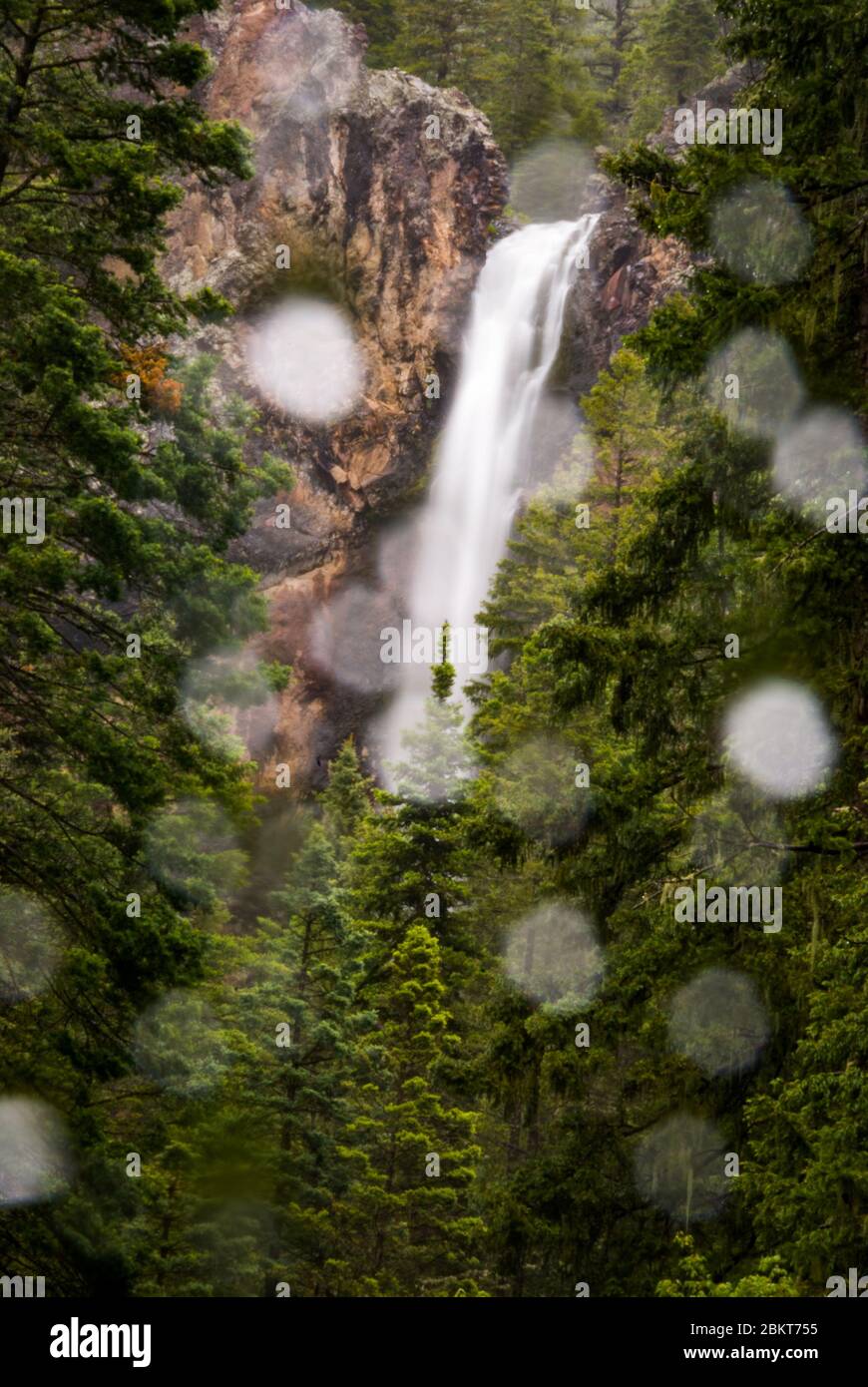 A huge, rushing waterfall seen through atmospheric rain among a dense ...