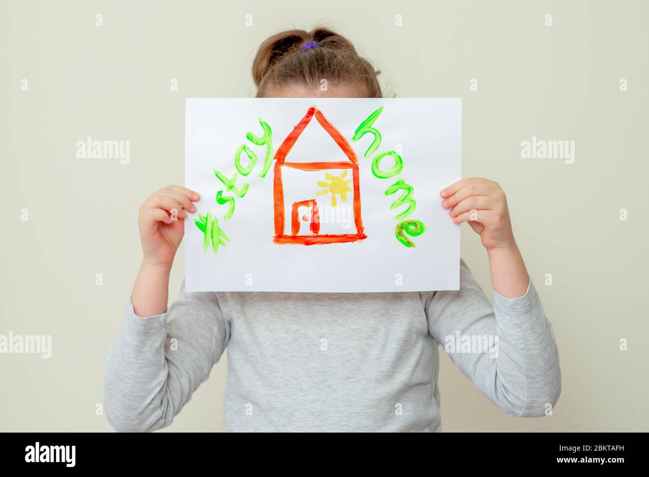 Hands of child holding a picture of red house and words Stay Home ...