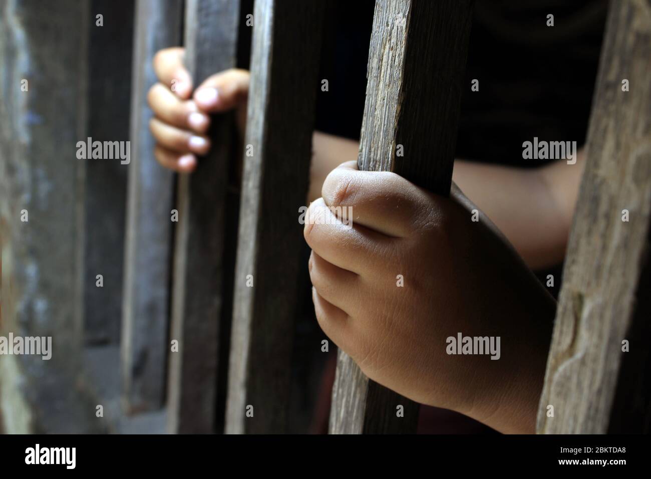 Hands of a young child clutching prison bars. Child in jail. Sad little ...