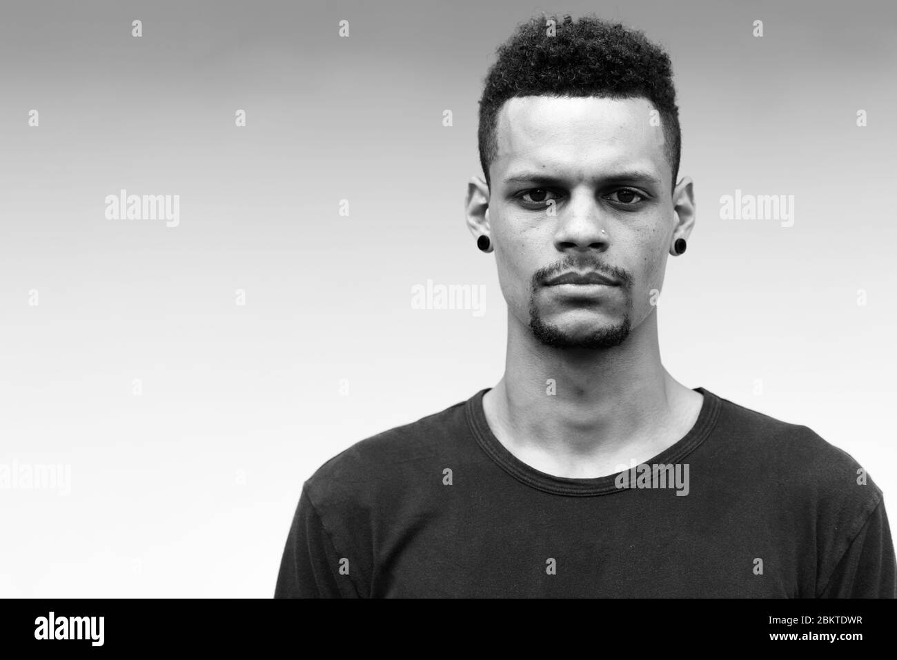 Face of young handsome bearded African man with earrings in black and ...