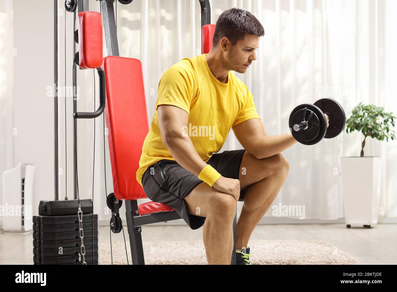 Man sitting on a fitness machine and exercising with a dumbbell at home ...