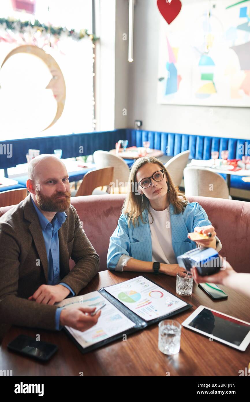 Fashionable businesswoman in glasses sitting with colleague at table ...
