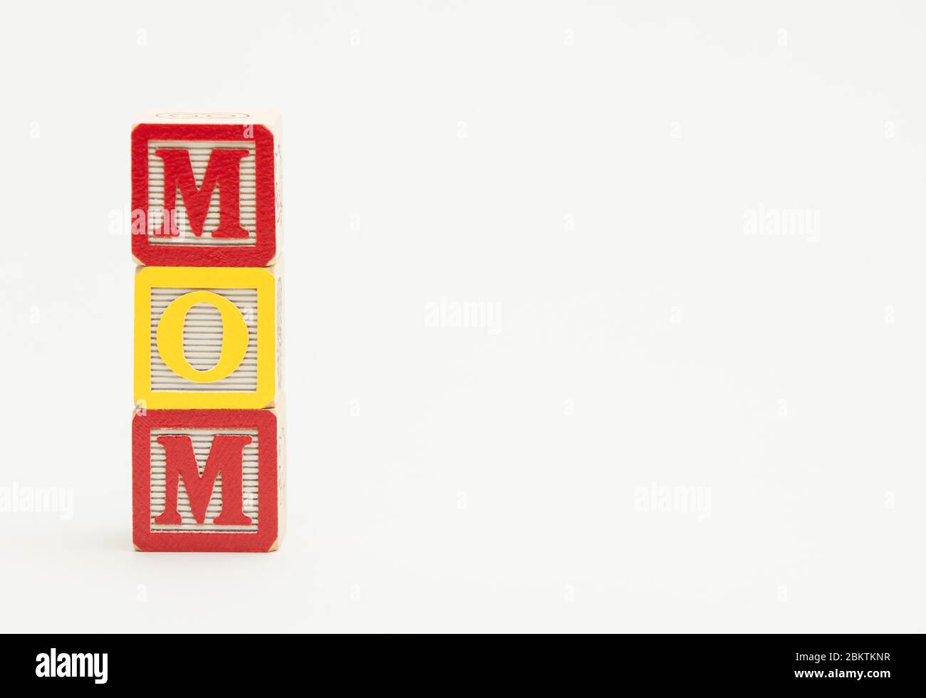 Three small wooden toy blocks spell the word mom in colorful letters on ...