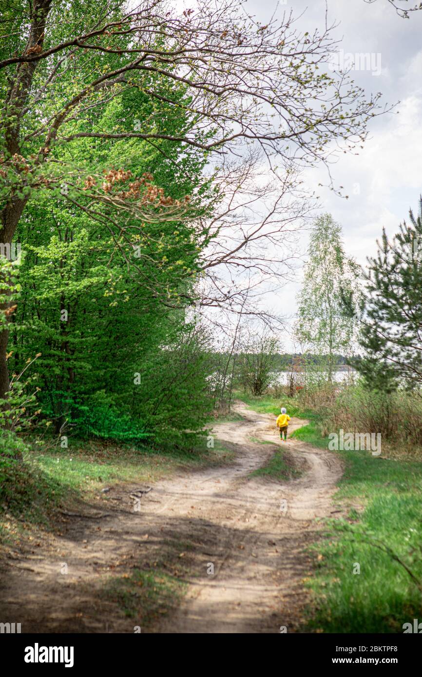 little kid in yellow coat running by forest trail footpath Stock Photo ...