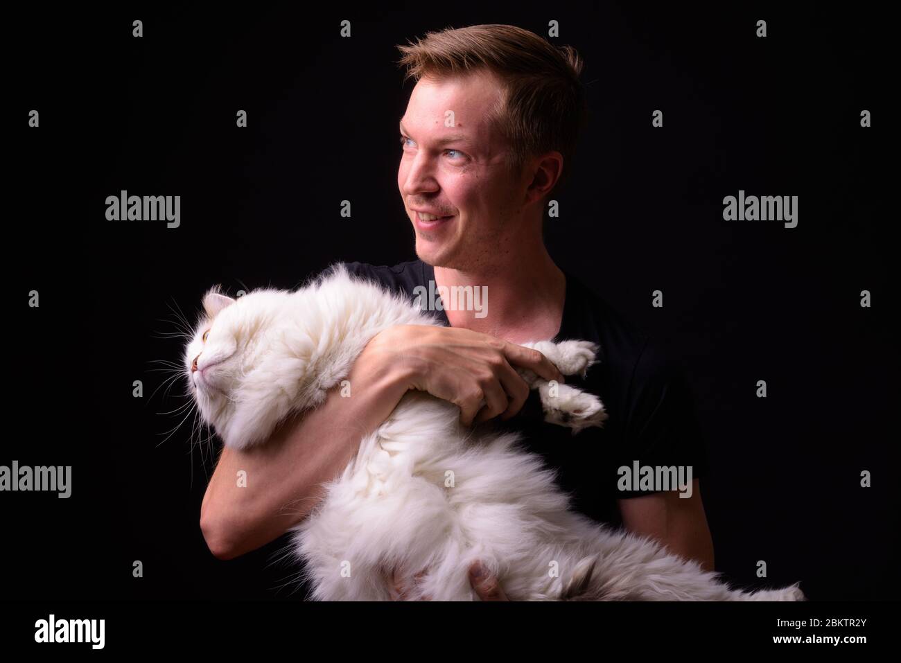Portrait of happy young handsome man thinking while holding Persian cat ...