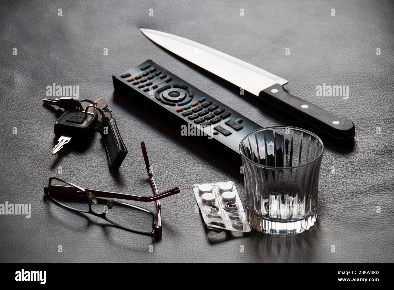 Still life with glasses, car keys, tablets, TV remote control and knife ...