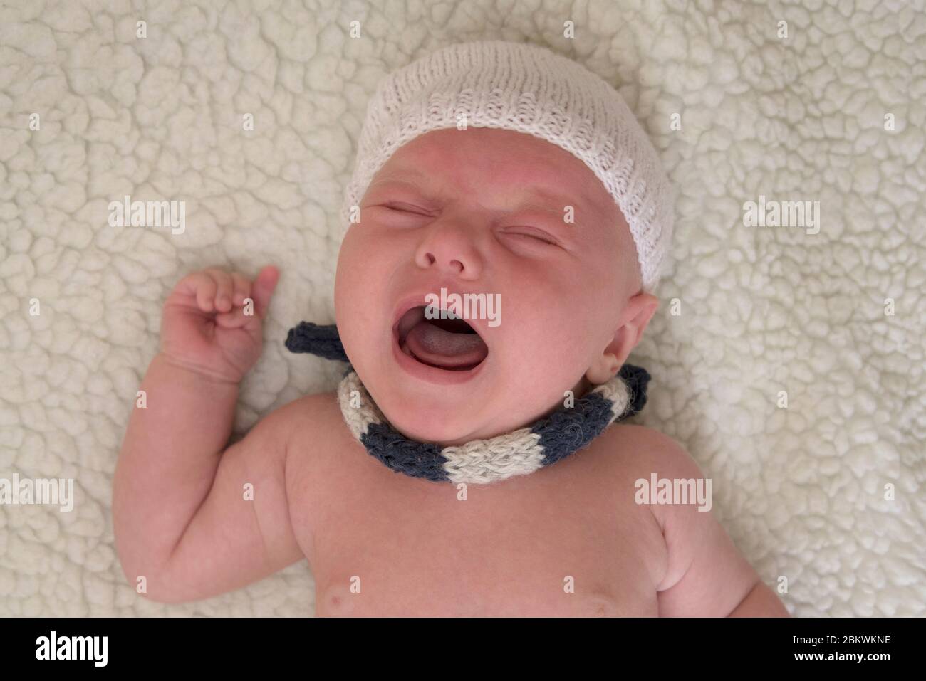 A newborn baby in a hat and scarf is crying on a light background Stock ...