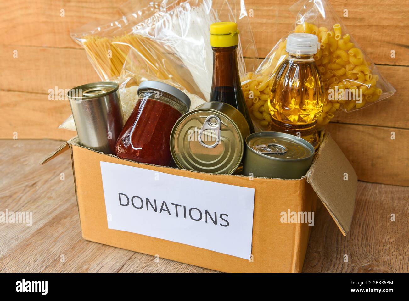 Donations box with canned food on wooden table background / pasta ...