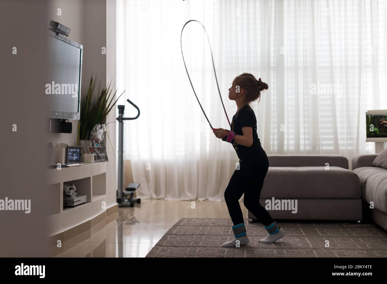 Happy little girl jumping over the rope at home during the isolation ...