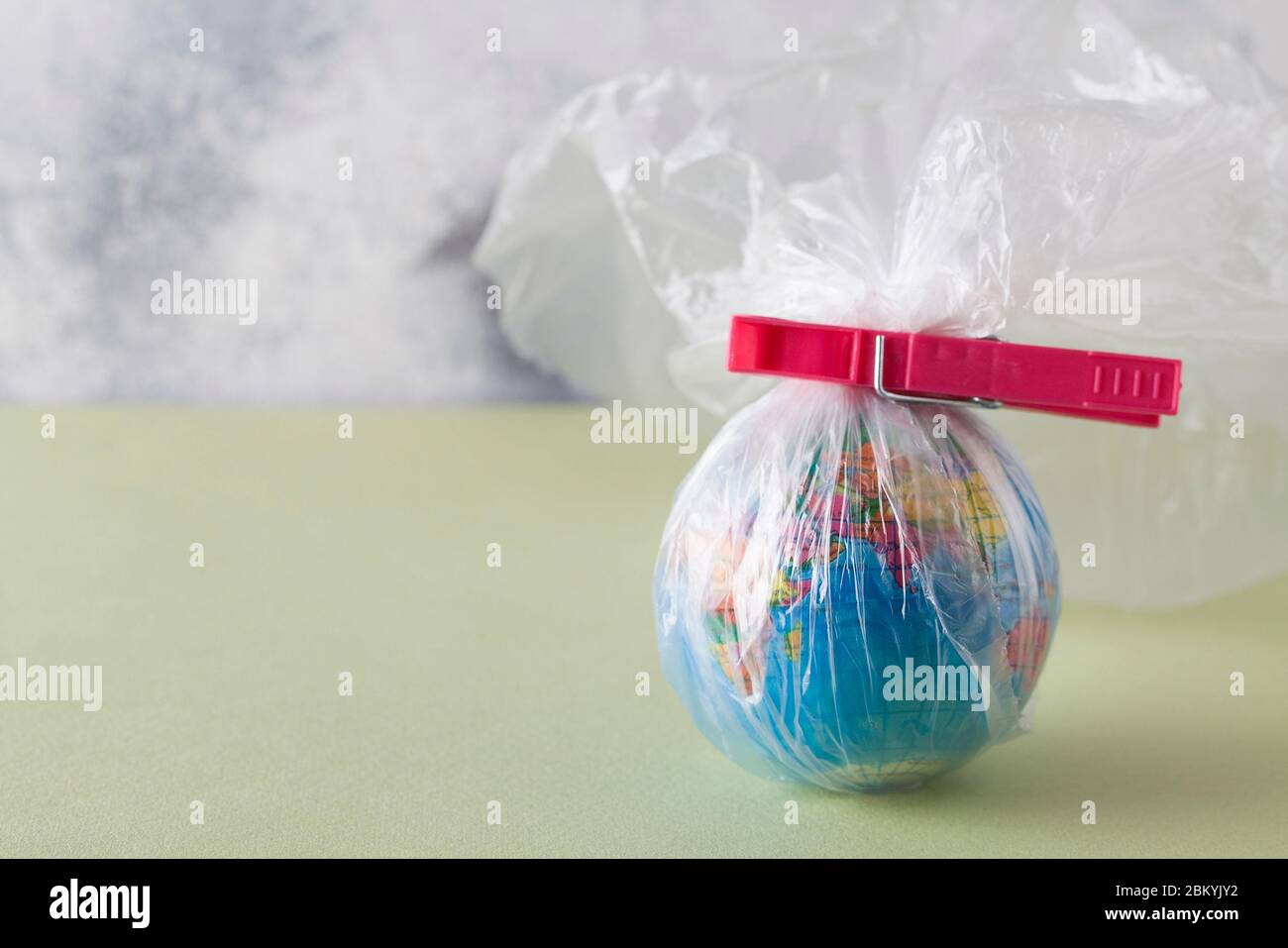 earth in plastic bag with pink pin on green background. Ecological ...