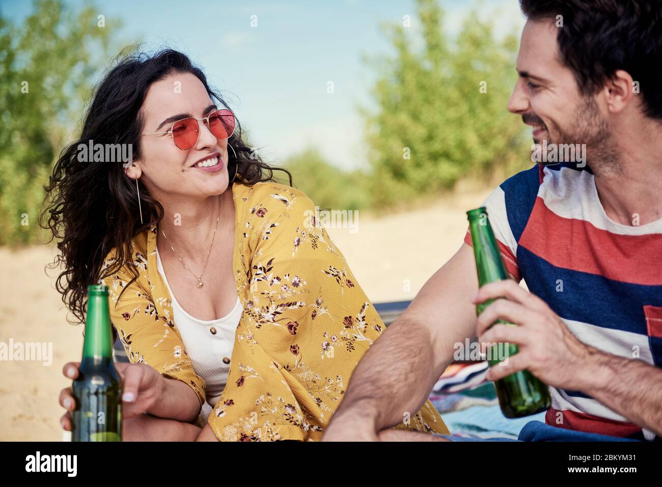 Smiling couple drinking cold beer on the beach Stock Photo - Alamy