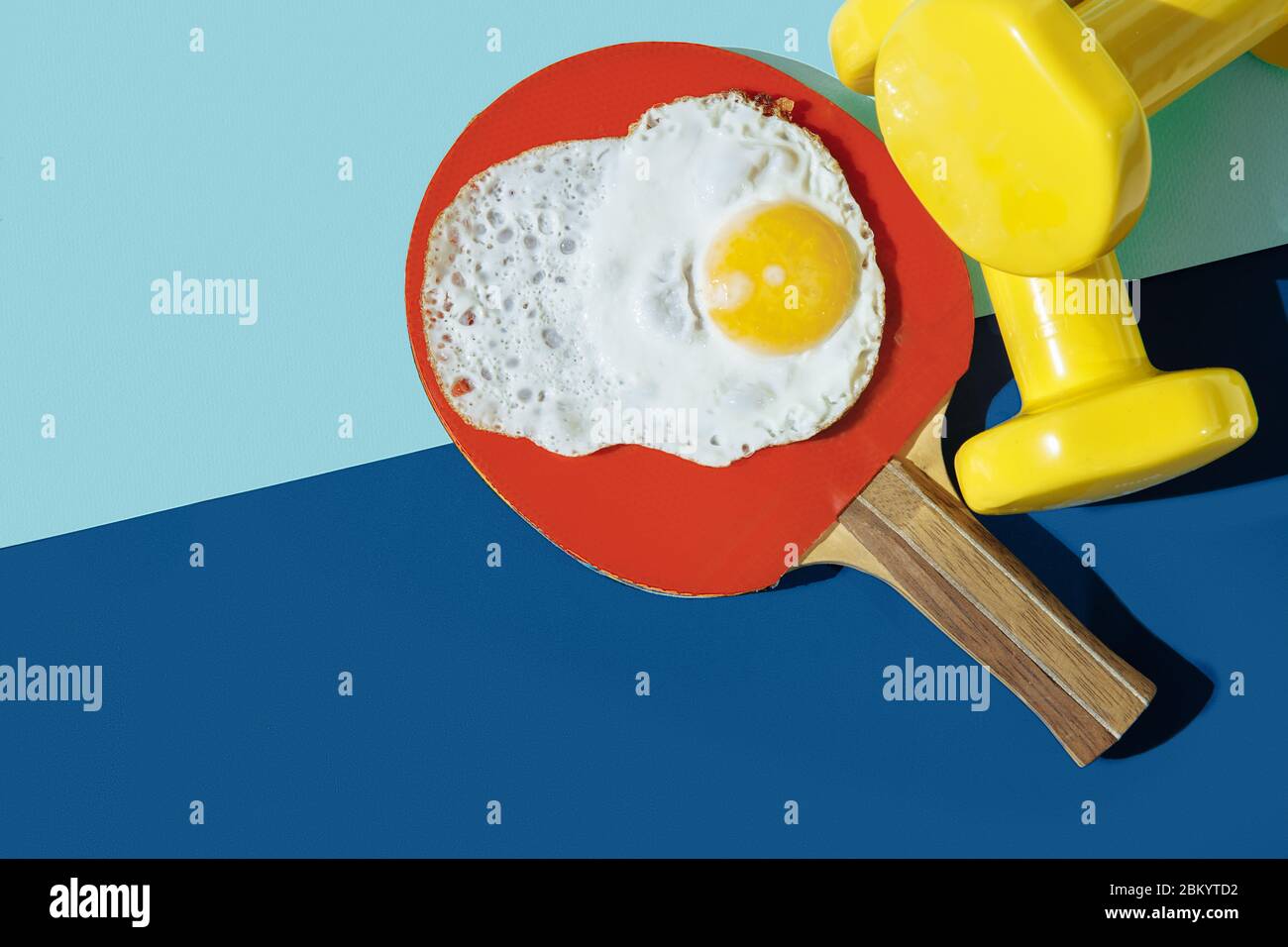 On the blue table are yellow dumbbells, a red ping pong racket, and ...
