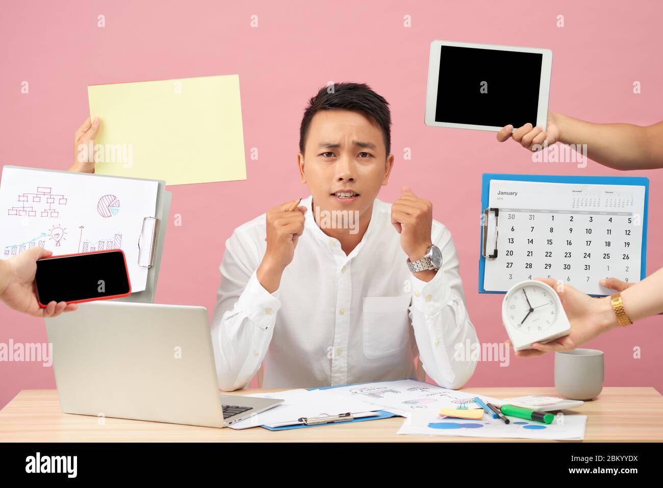 Sad young man sits at desktop, hands with papers, alarm clock, touchpad ...