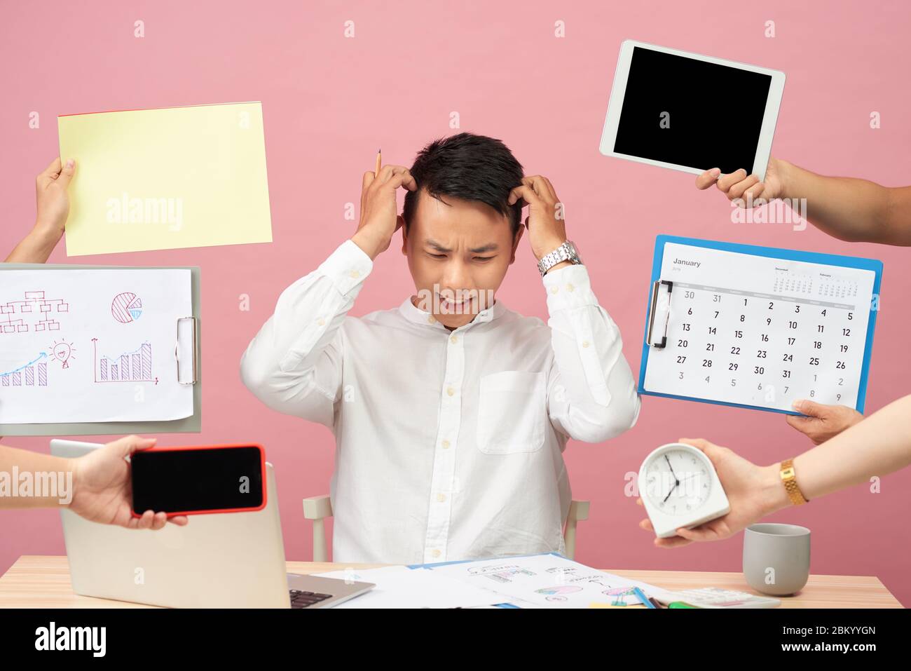 Sad young man sits at desktop, hands with papers, alarm clock, touchpad ...