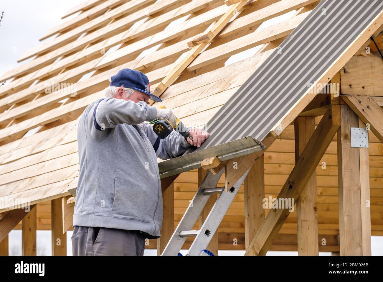 Senior Construction man using a screwdriver, fastens a roofing sheet to ...