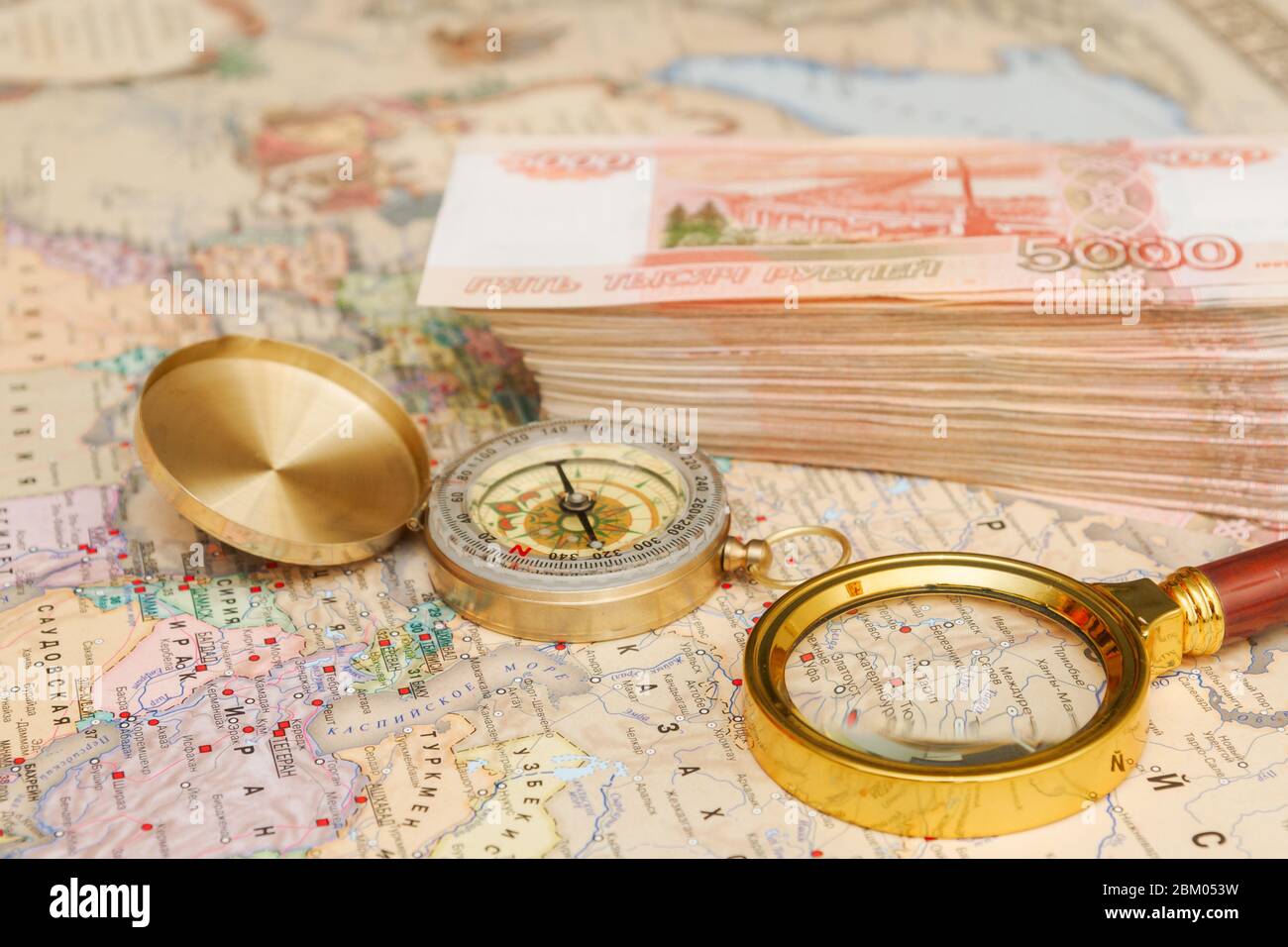 A compass with a bundle of big money and a magnifying glass are on the ...