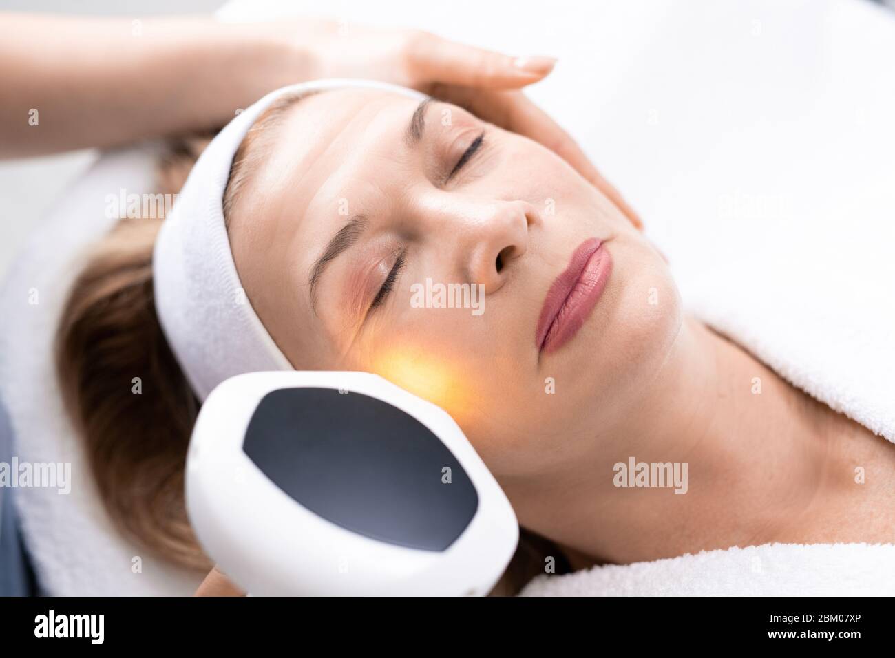 Hand of beautician using laser handle on mature womens face while ...