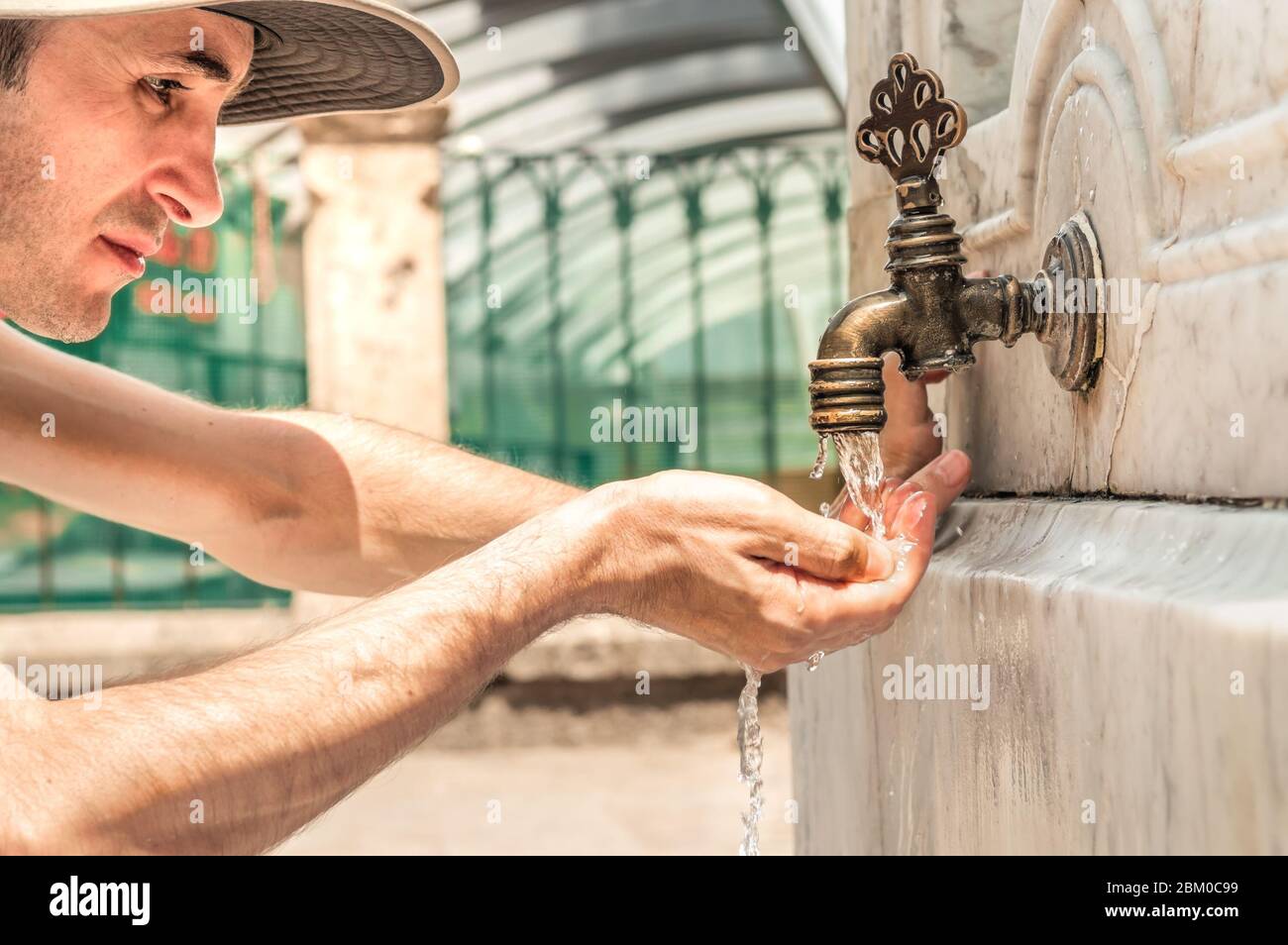 Young man drinking water with his hand from an antique Turkish fountain ...