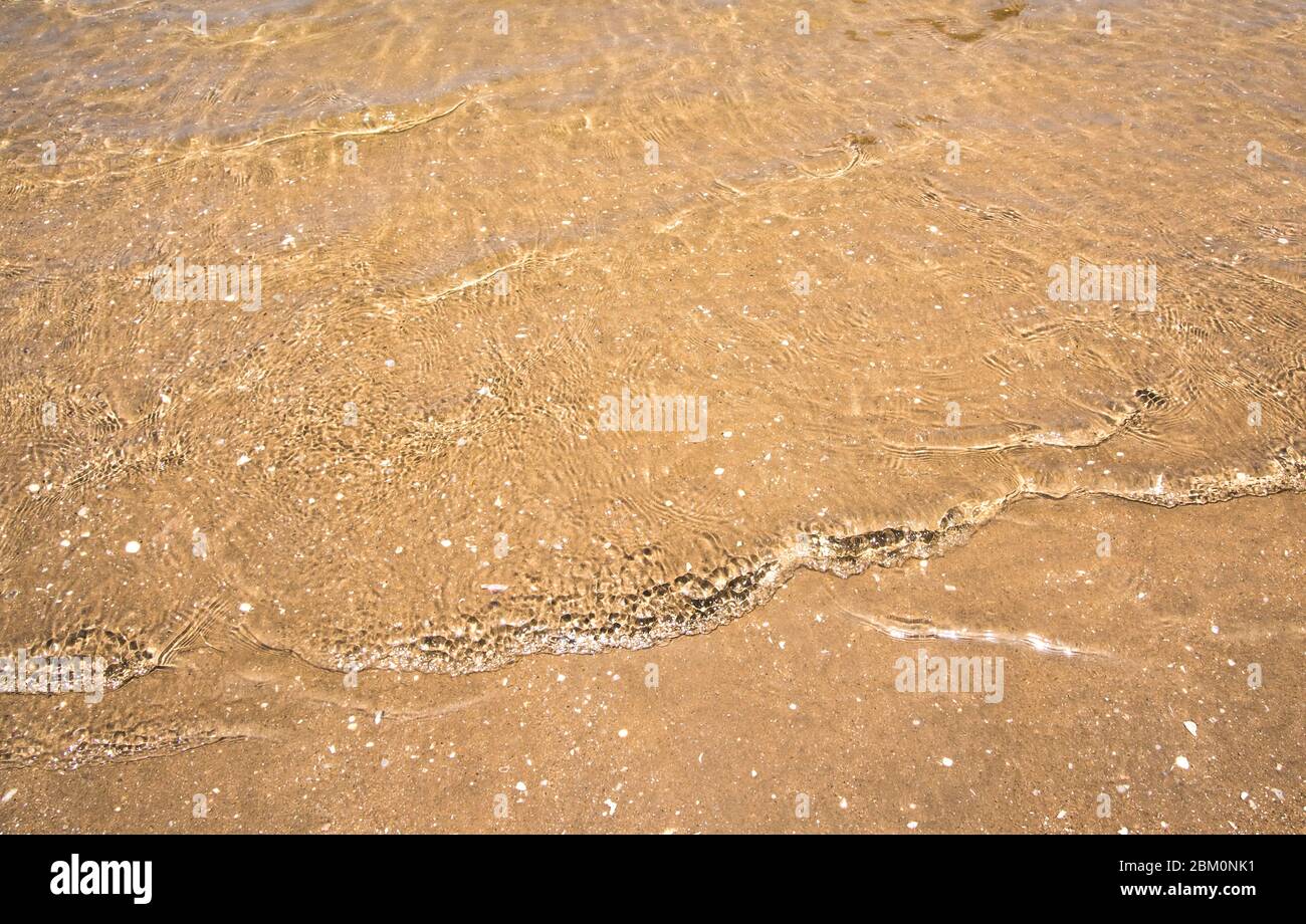 Reflection of sunlight on the moving sea water surface, sand beach and ...