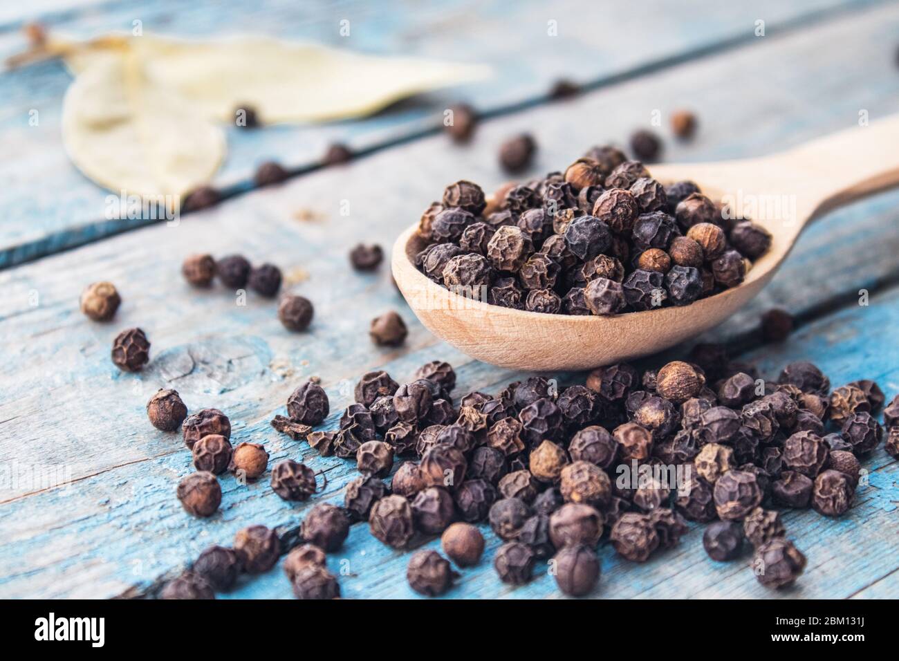 Dry black pepper in a wooden spoon near black pepper scattered on blue ...