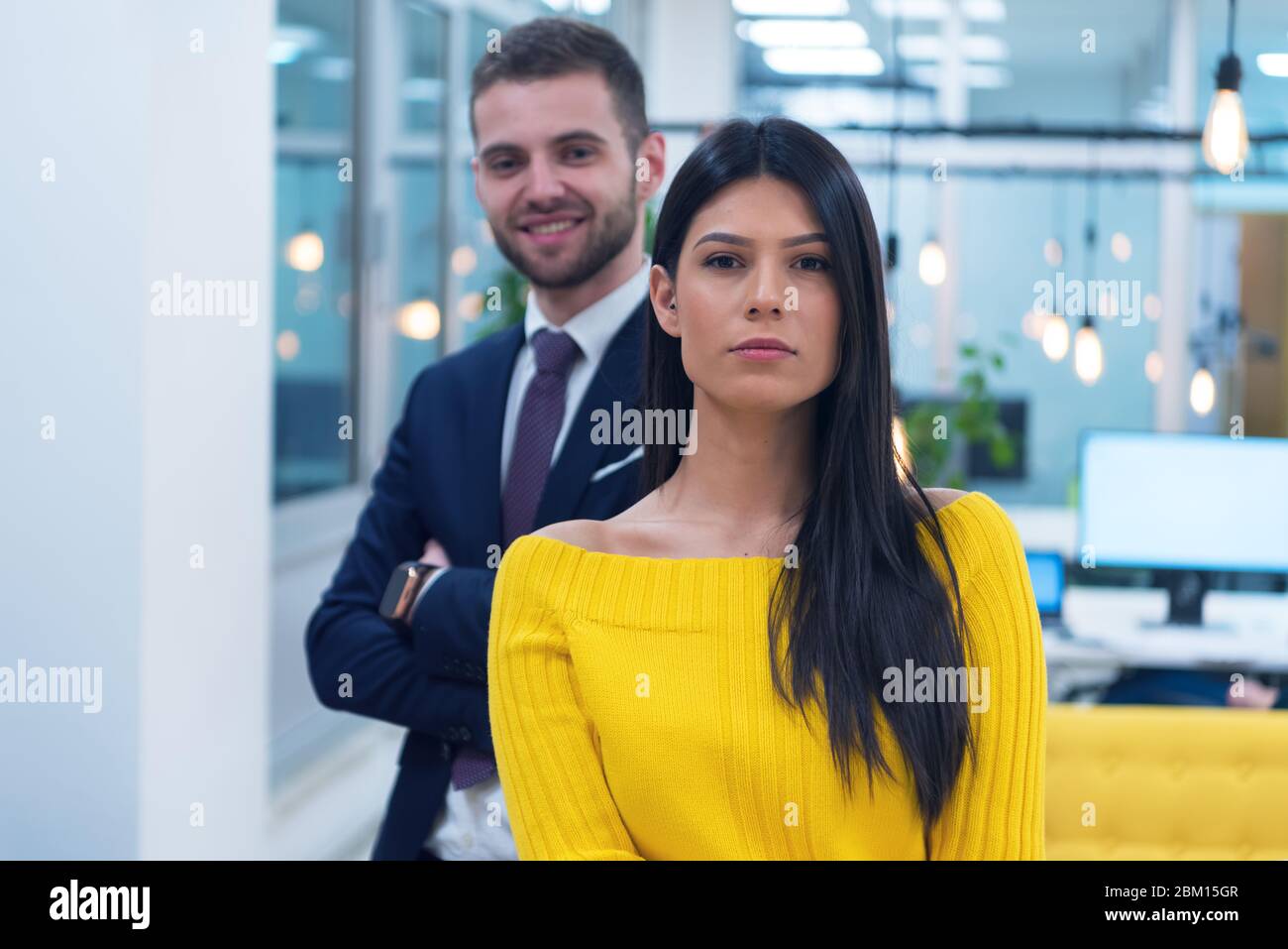 Portrait of two young co workers standing at workplace inside modern co ...