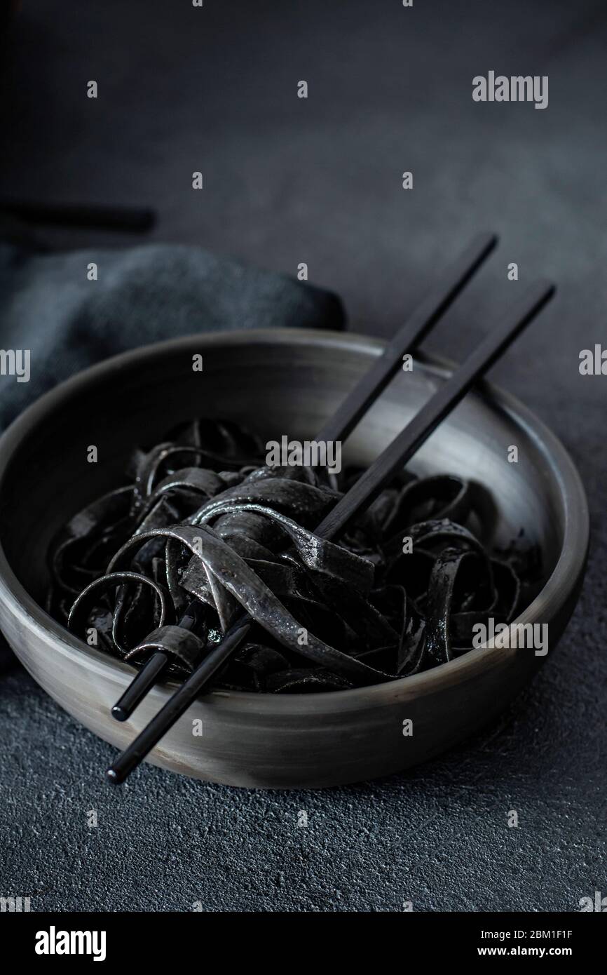 Black pasta with cuttlefish ink in a black plate on a black background ...