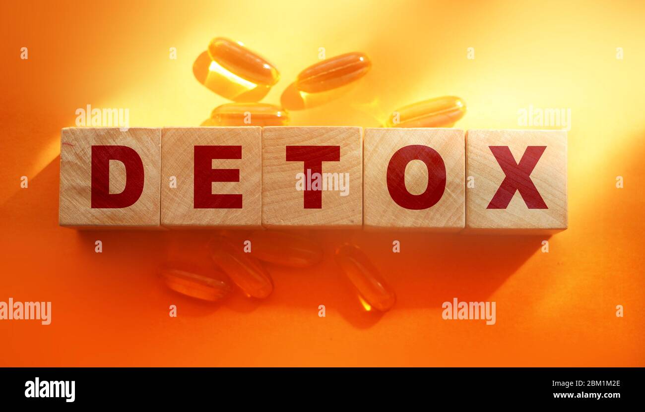 Detox word made with wooden blocks and oil capsuless around on orange ...